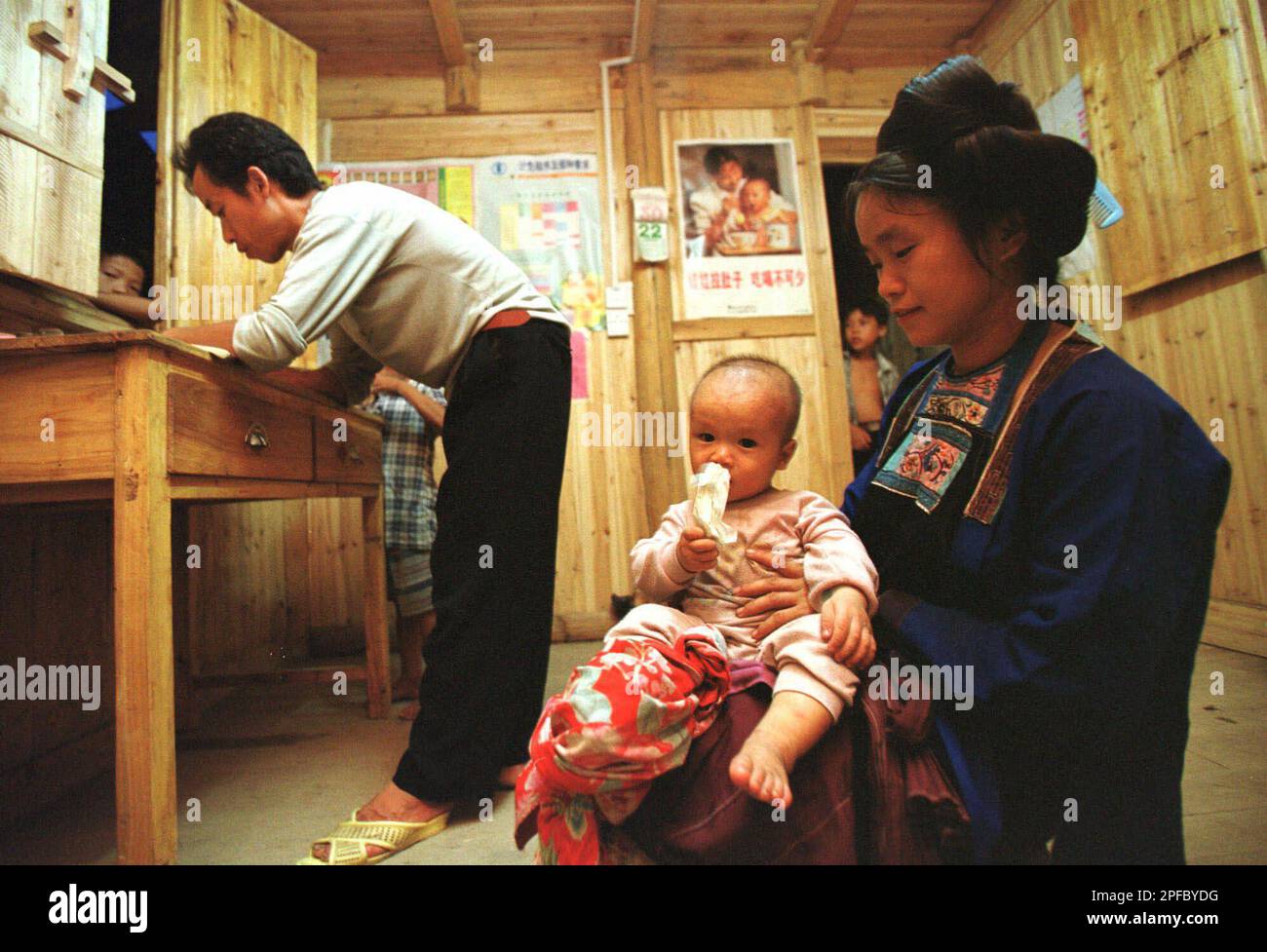 A young mother, of the Miao ethnic minorioty, waits with her baby as ...