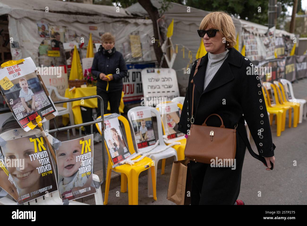 A woman walks next to photos of Shiri Bibas and her sons Ariel and Kfir ...