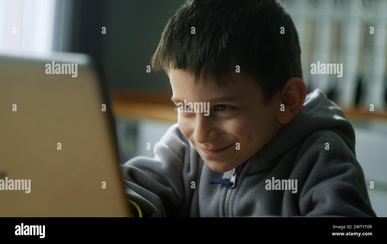 Primo piano di un bambino seduto in cucina usando il computer portatile ...