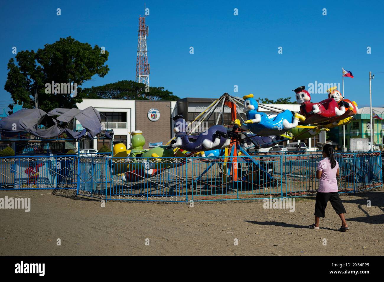 A woman walks past a carnival ride in front of the town municipal hall ...