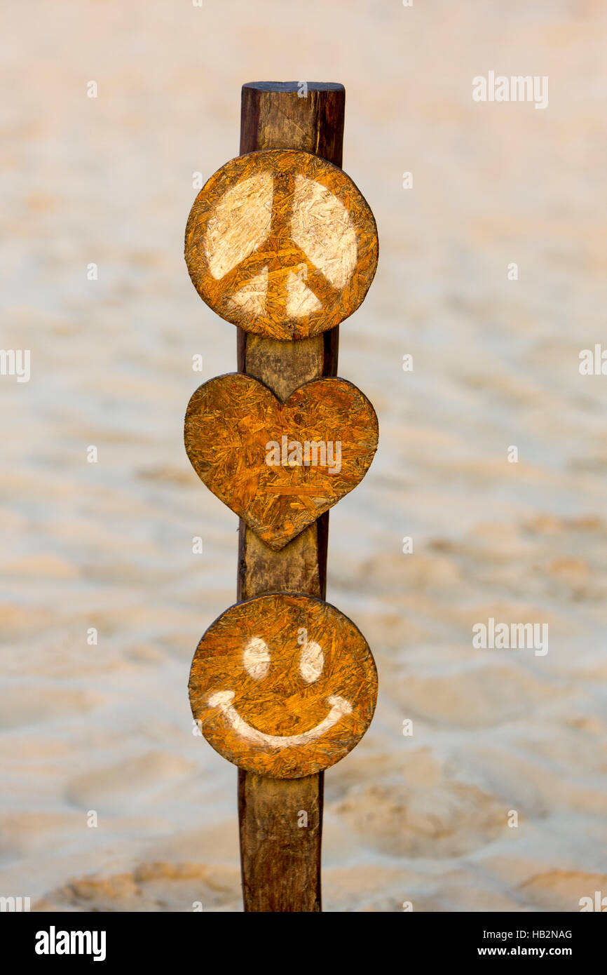 Cartello in legno con la pace, di cuore e di uno smiley sulla spiaggia ...