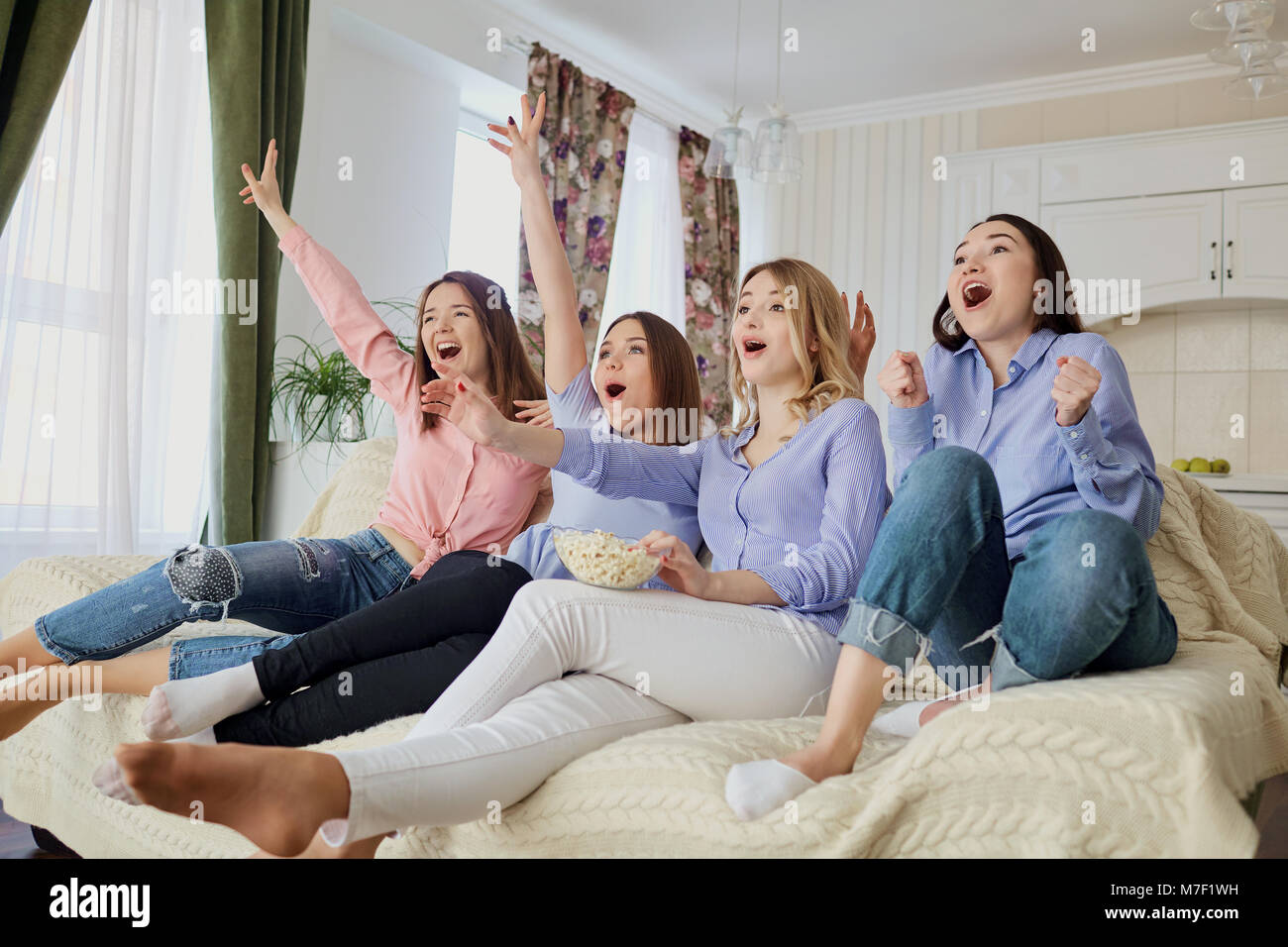Le ragazze giovani guardano la TV, mangiare popcorn seduta sul divano ...