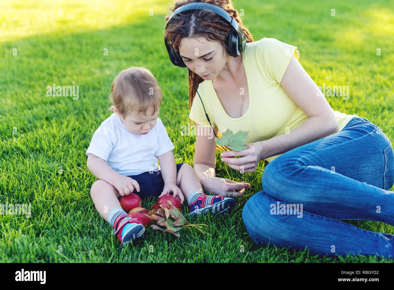 Bellissima giovane mamma moderna nelle cuffie giocando in un prato ...