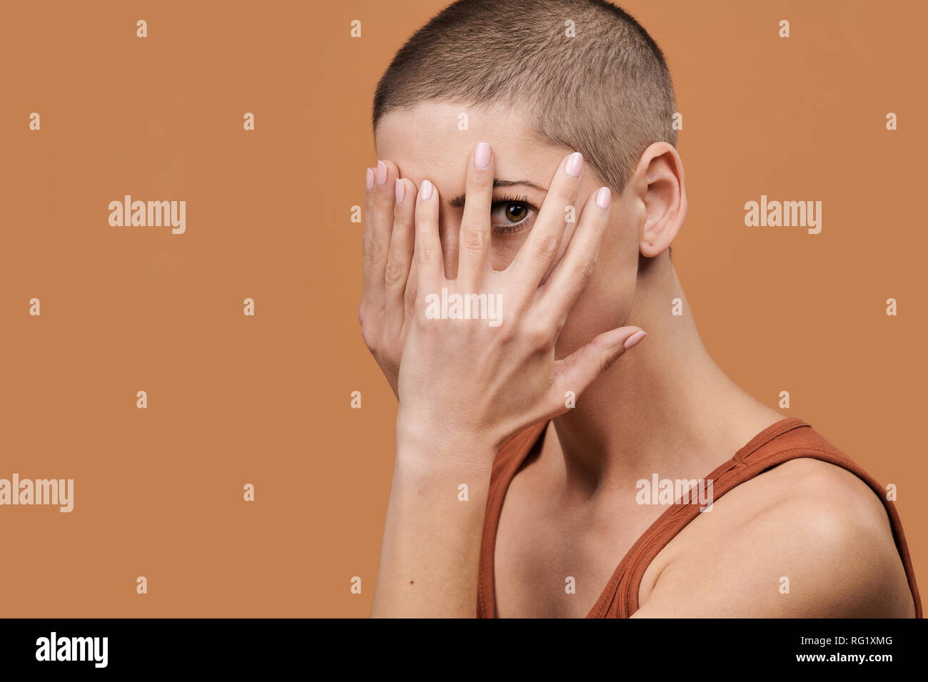Bella giovane donna con la testa rasata che copre il volto con entrambe ...